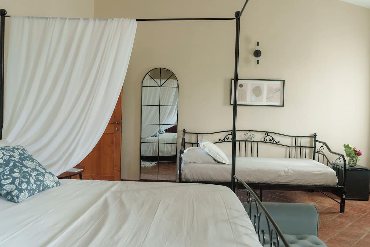 Quarto com cama de dossel, cama menor, espelho e quadro na parede.