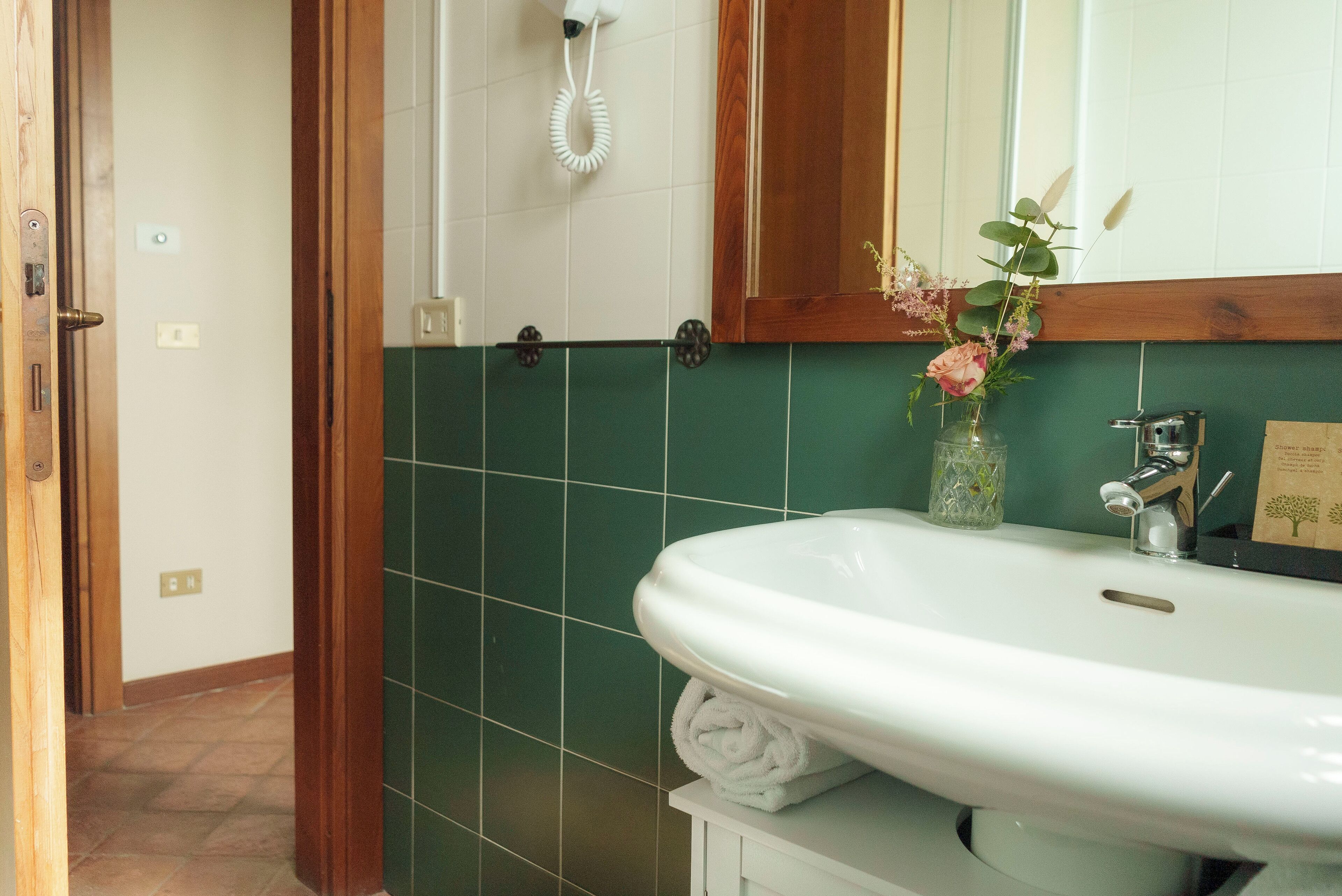 Um banheiro com pia branca, azulejos verdes, moldura de porta de madeira e uma toalha no balcão.