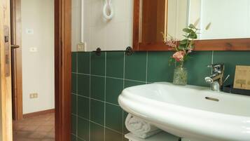 Um banheiro com pia branca, azulejos verdes, moldura de porta de madeira e uma toalha no balcão.