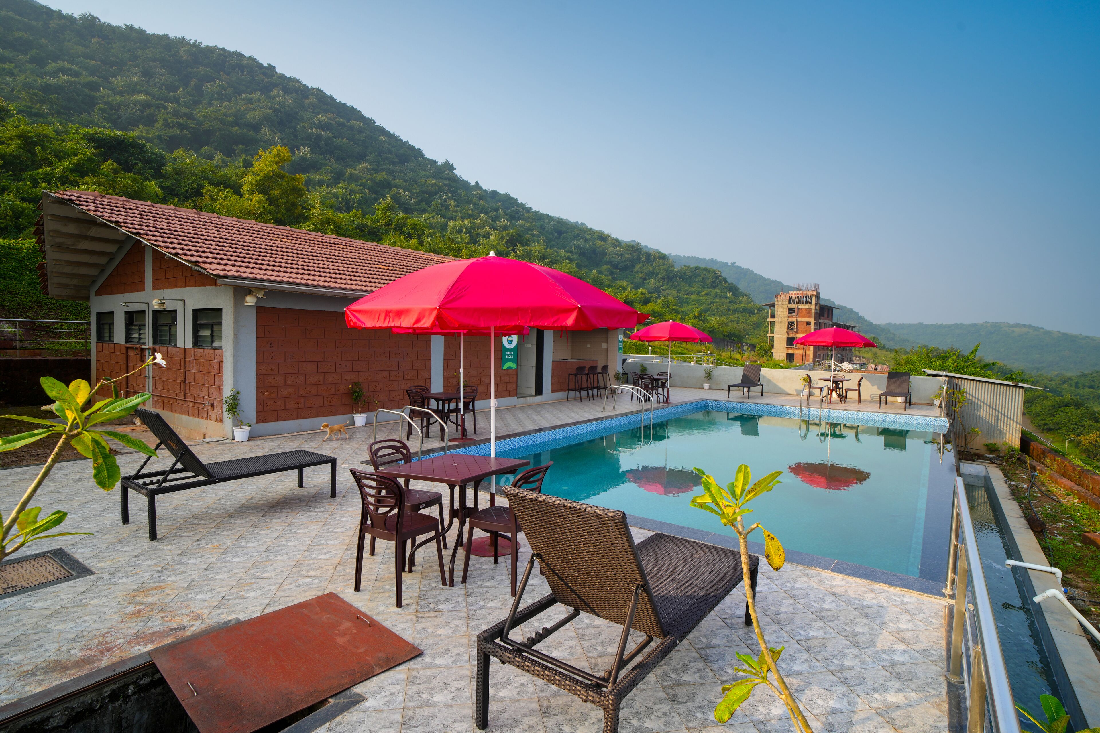 Área de piscina com espreguiçadeiras, mesa e guarda-sóis vermelhos.