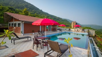 Área de piscina com espreguiçadeiras, mesa e guarda-sóis vermelhos.