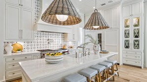 Cozinha moderna com armários brancos, ilha de mármore e banquetas de vime.