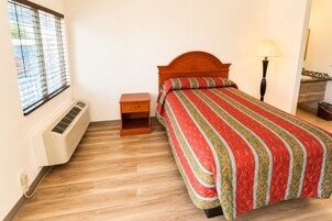 Quarto com cama, mesa de cabeceira, luminária e ar condicionado.