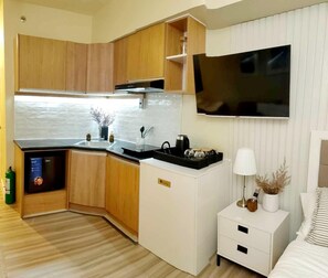 Cozinha compacta com armários de madeira, bancada preta e TV integrada.