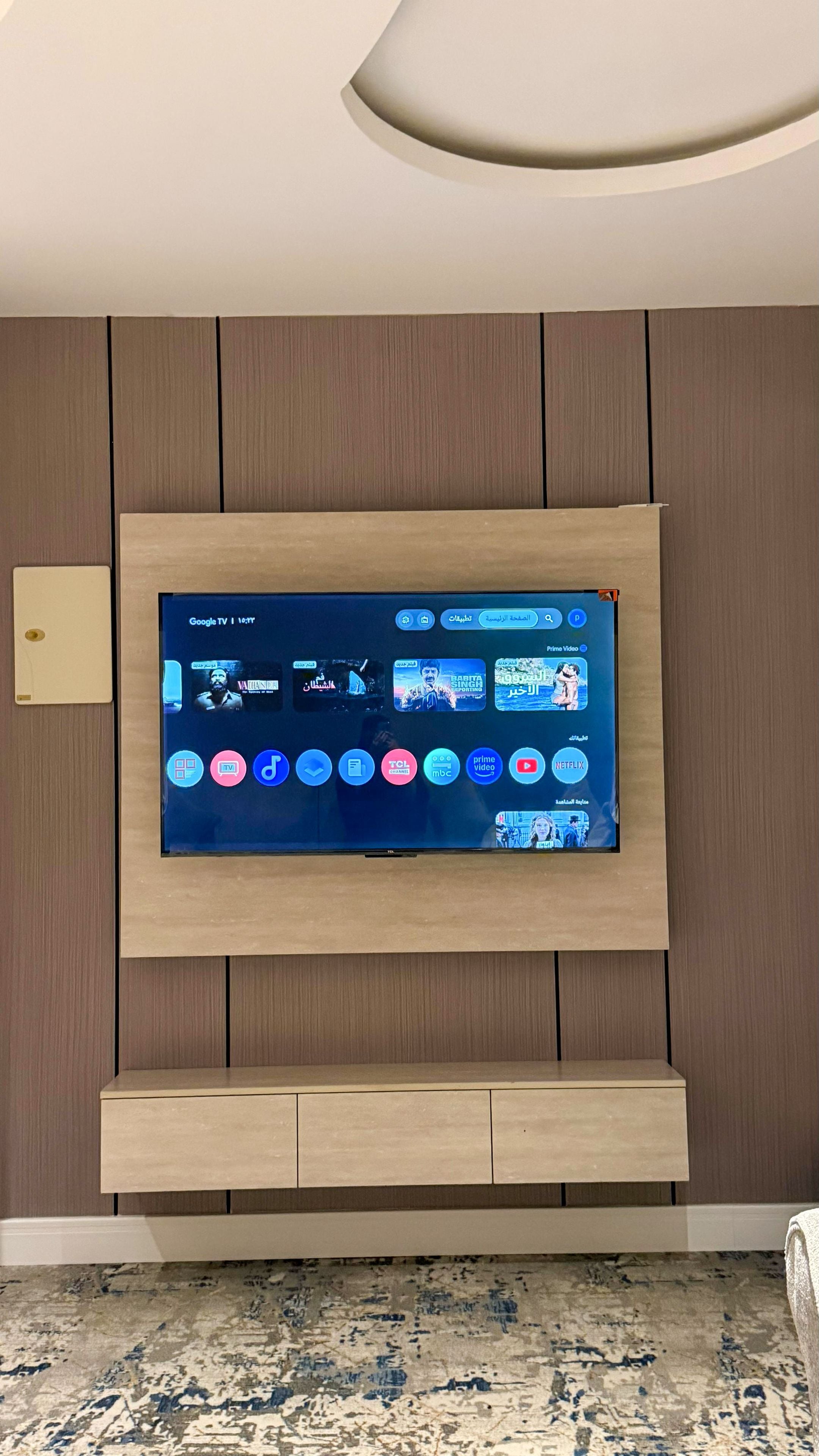Televisão de tela plana fixada na parede com detalhe em painel de madeira.
