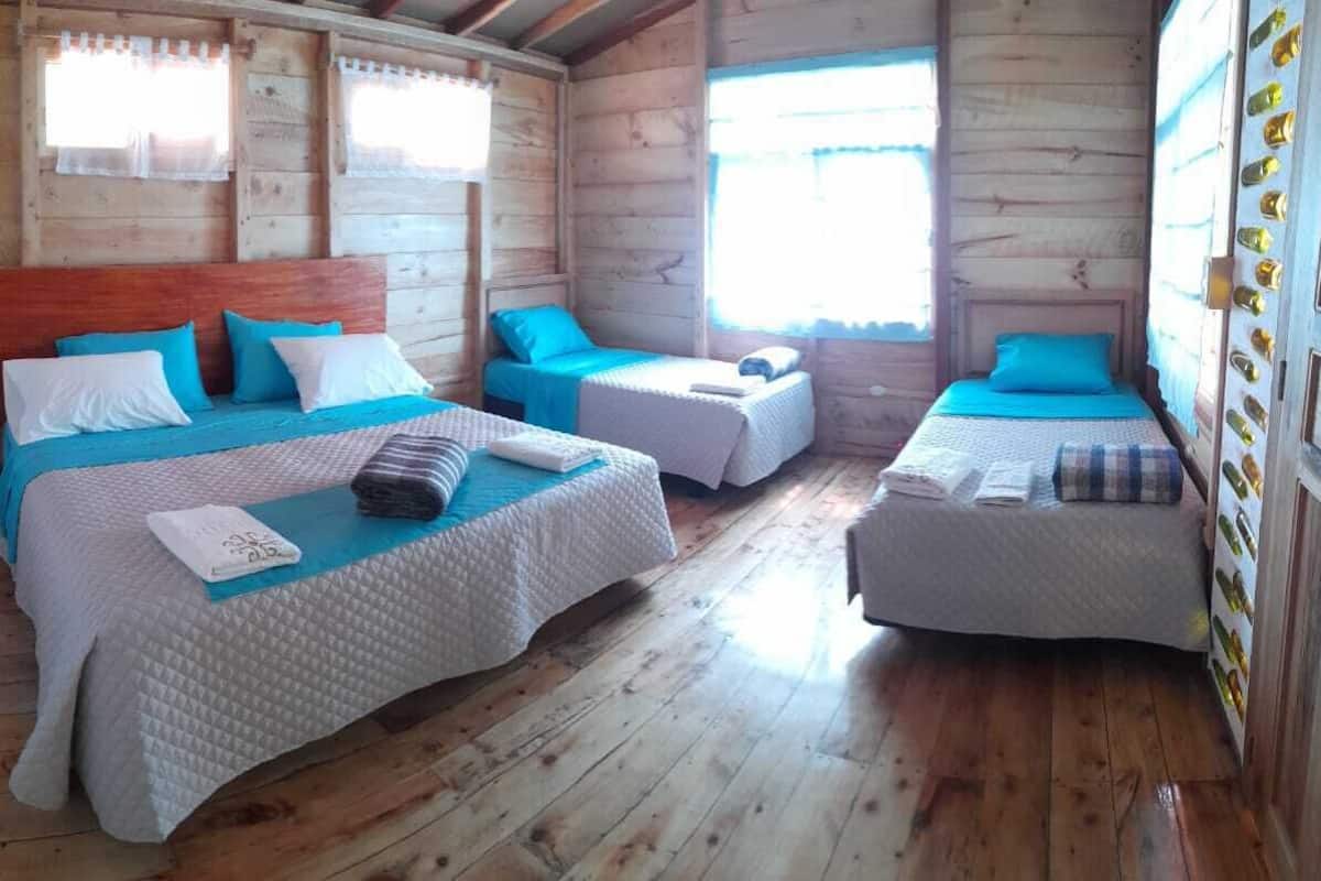 Uma cabana de madeira com três camas, cada uma com roupa de cama azul e branca.