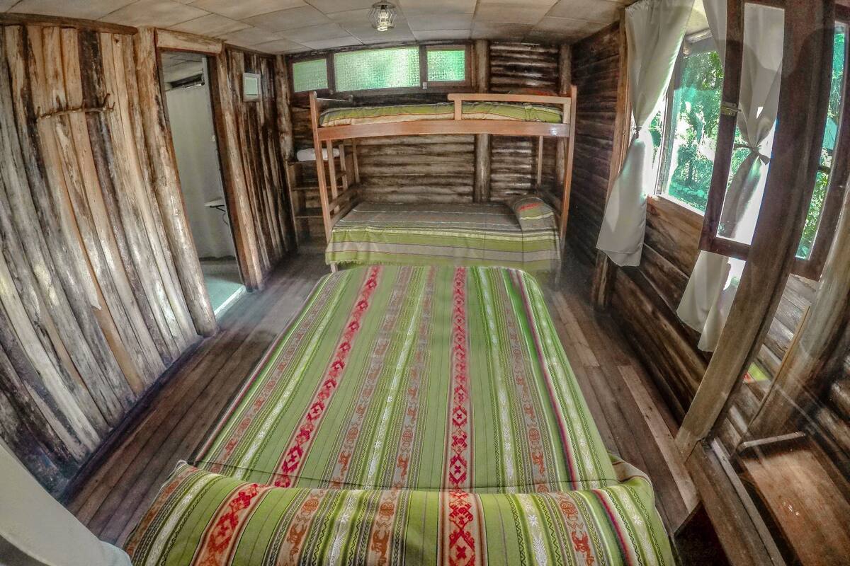 Uma cabana rústica com beliche, paredes de madeira e uma janela com cortinas.