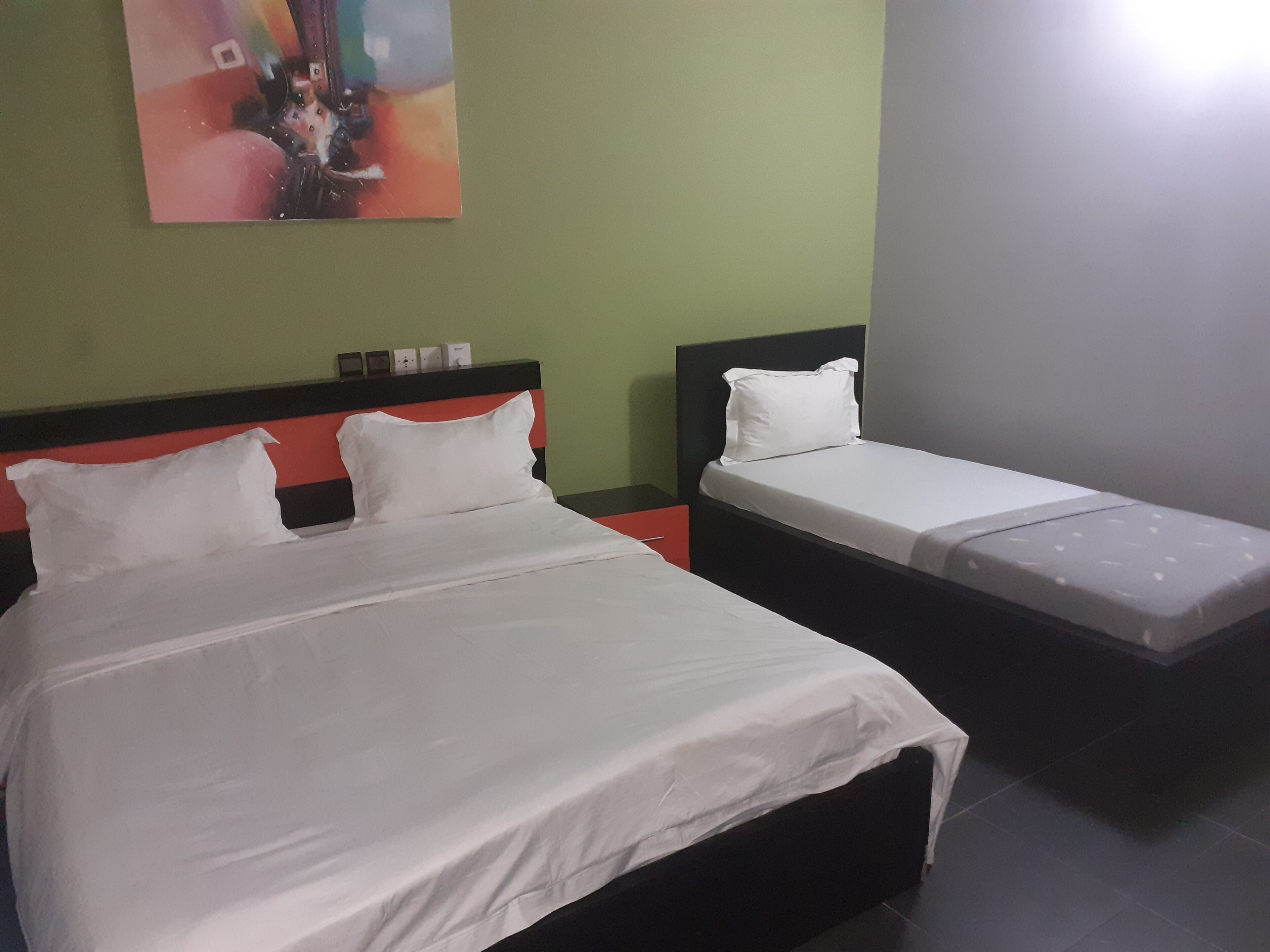 Quarto de hotel com uma cama grande, uma cama menor e uma mesa de cabeceira com abajur.
