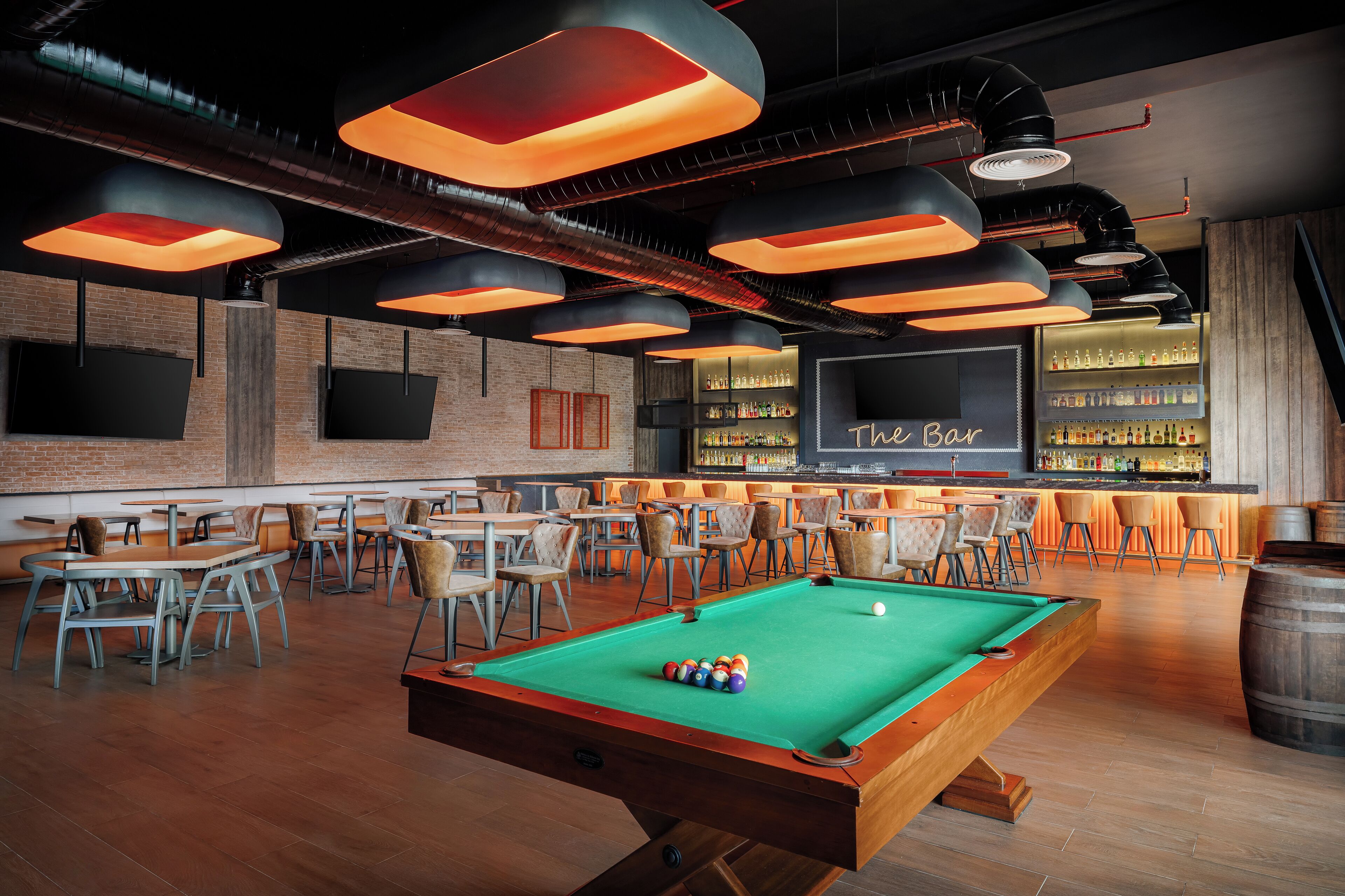 Uma área de bar com mesa de bilhar, assentos e balcão com diversas garrafas.