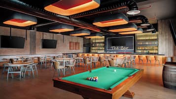 Uma área de bar com mesa de bilhar, assentos e balcão com diversas garrafas.