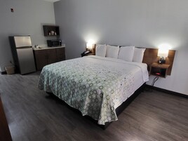 Quarto de hotel com cama, abajures, escrivaninha com micro-ondas e um pequeno frigorífico.