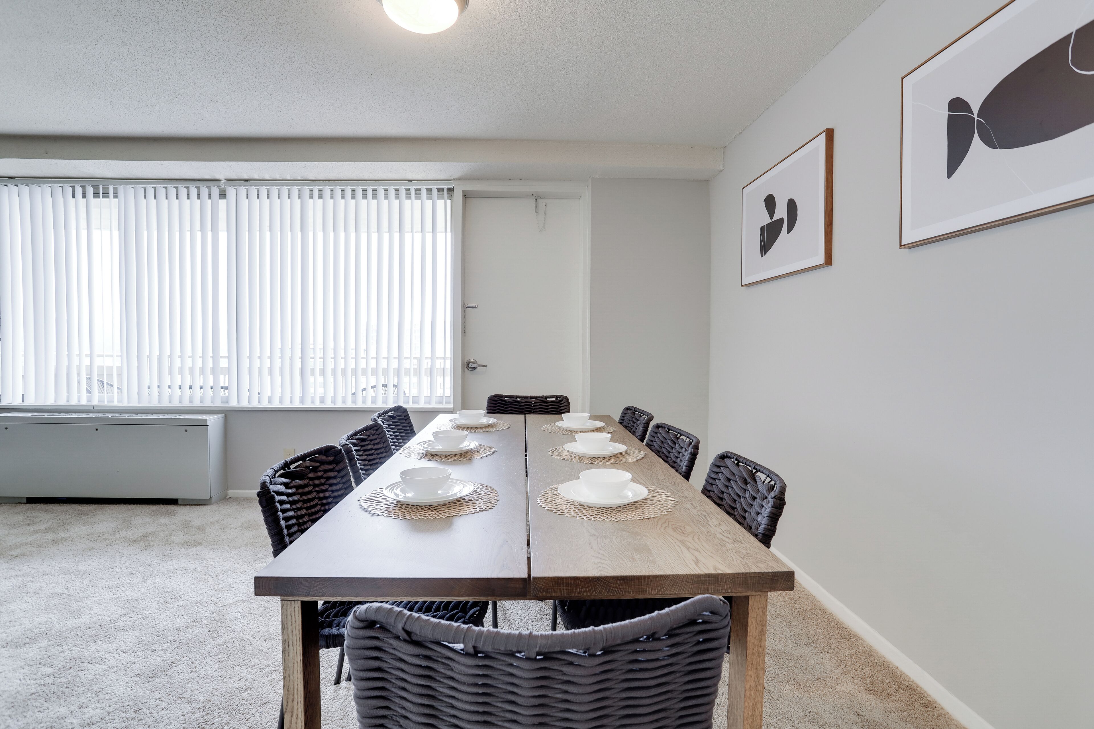 Uma sala de jantar com uma longa mesa de madeira posta para seis pessoas, cercada por cadeiras de vime.