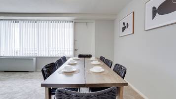 Uma sala de jantar com uma longa mesa de madeira posta para seis pessoas, cercada por cadeiras de vime.