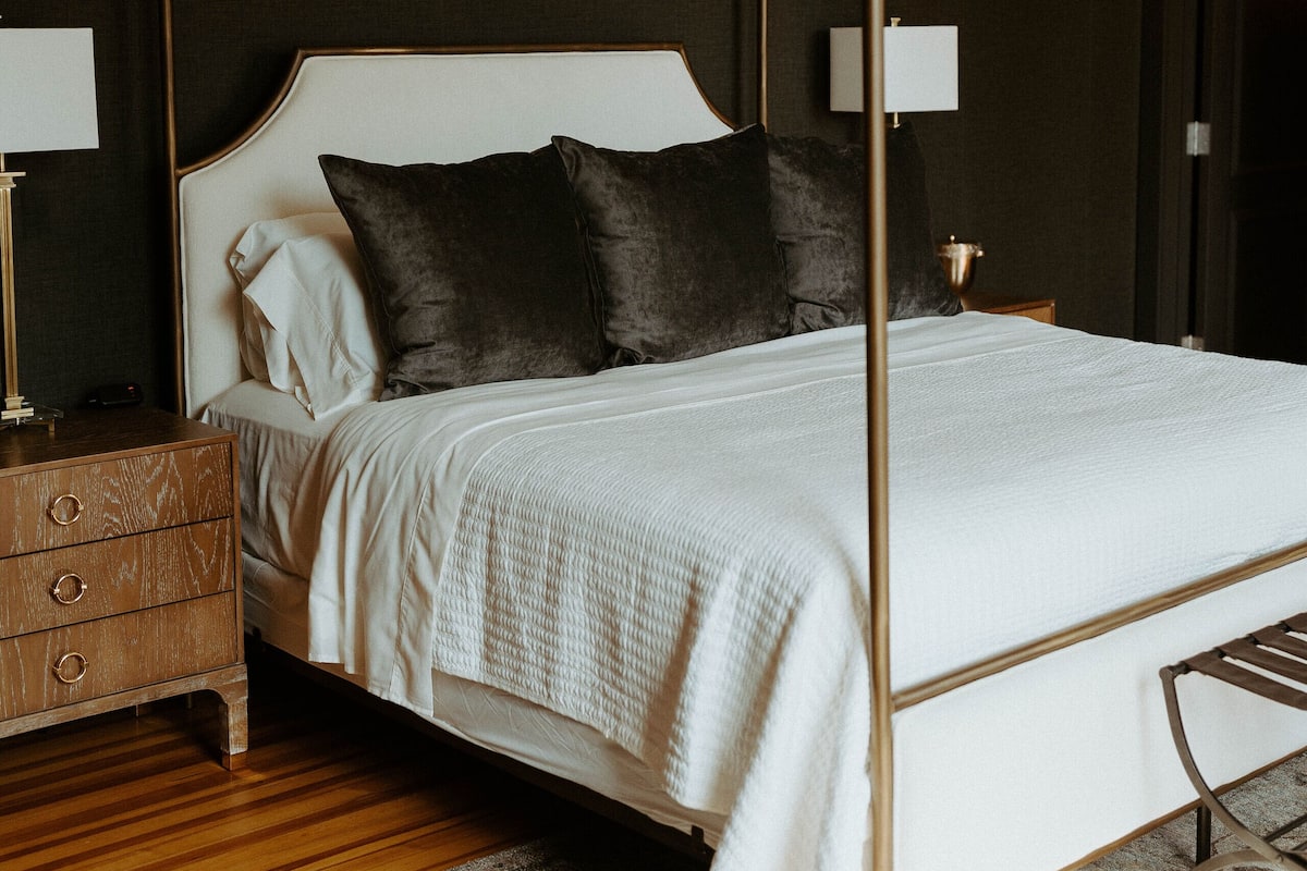 Quarto moderno com cama de dossel, mesa de cabeceira de madeira e tapete estampado.