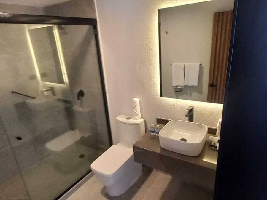 Uma casa de banho moderna com cabine de duche em vidro, sanita e lavatório com espelho em cima.