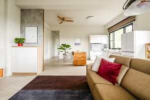 Uma sala de estar moderna com um sofá, uma mesa de centro e uma almofada vermelha. Há um armário de madeira e uma planta em vaso no canto.