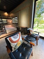 Quarto moderno com beliches, mesa de jantar e dois sofás de couro com almofadas.