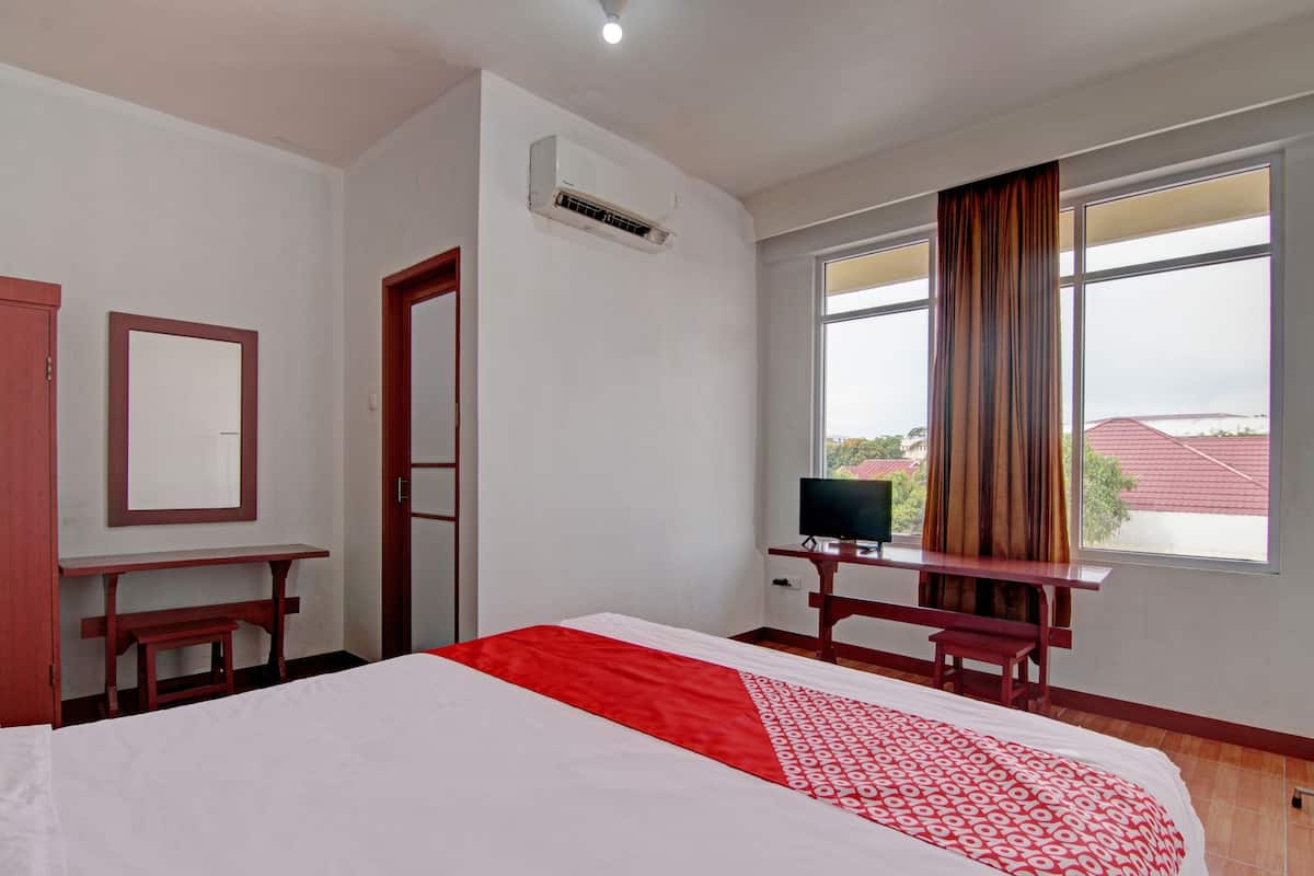 Quarto de hotel com cama, escrivaninha, televisão e janela com cortinas.