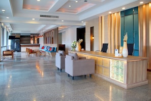 Um lobby moderno de hotel com balcão de recepção, área de estar e uma grande janela.