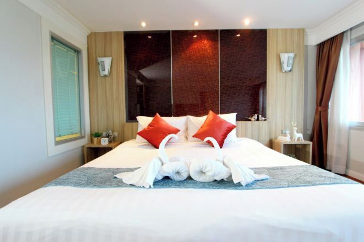 Quarto de hotel com uma cama grande, almofadas vermelhas e arranjo de toalhas sobre a cama.