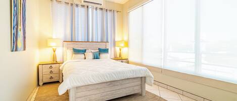 Quarto com uma cama grande, duas mesas de cabeceira com luminárias, um ventilador de teto e uma janela ampla.