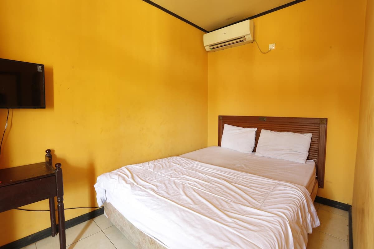Quarto com uma cama, mesa de cabeceira de madeira e televisão fixada na parede.