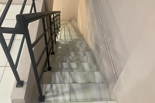 Uma escada com corrimão de metal, degraus azulejados e uma parede lisa.