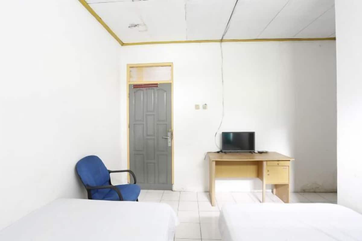 Quarto com duas camas, uma escrivaninha com computador, uma cadeira e uma porta.