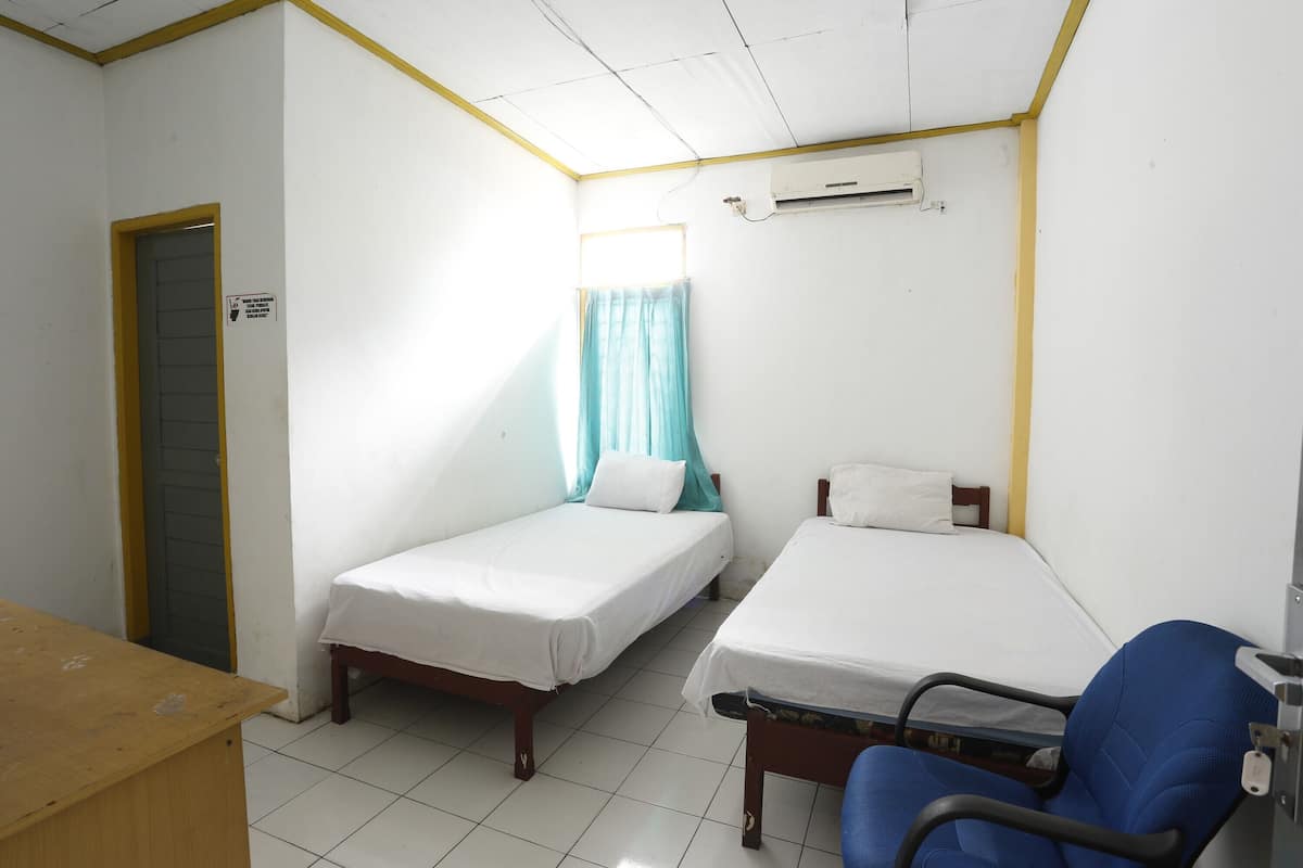 Quarto com duas camas de solteiro, uma escrivaninha de madeira, uma cadeira azul e uma janela com cortina.
