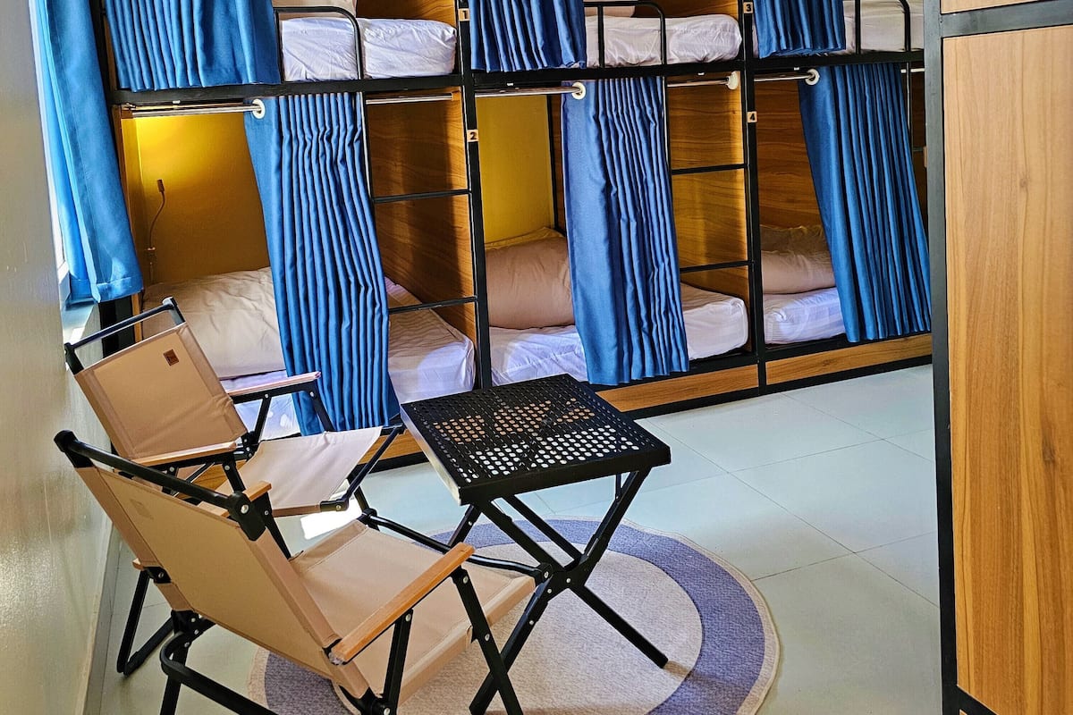 Quarto compacto com beliches, uma cadeira dobrável e uma pequena mesa.