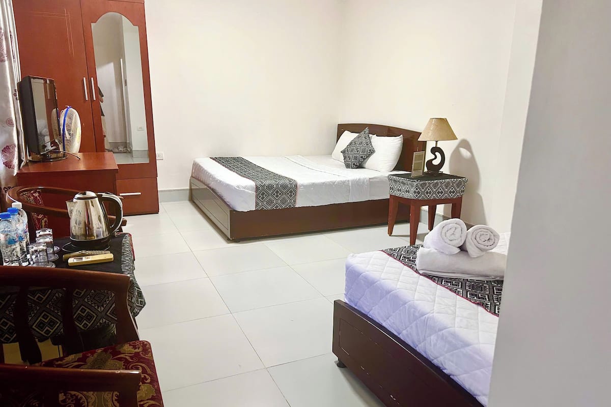Quarto de hotel com cama, uma cadeira, uma mesinha de cabeceira com abajur e um guarda-roupa.