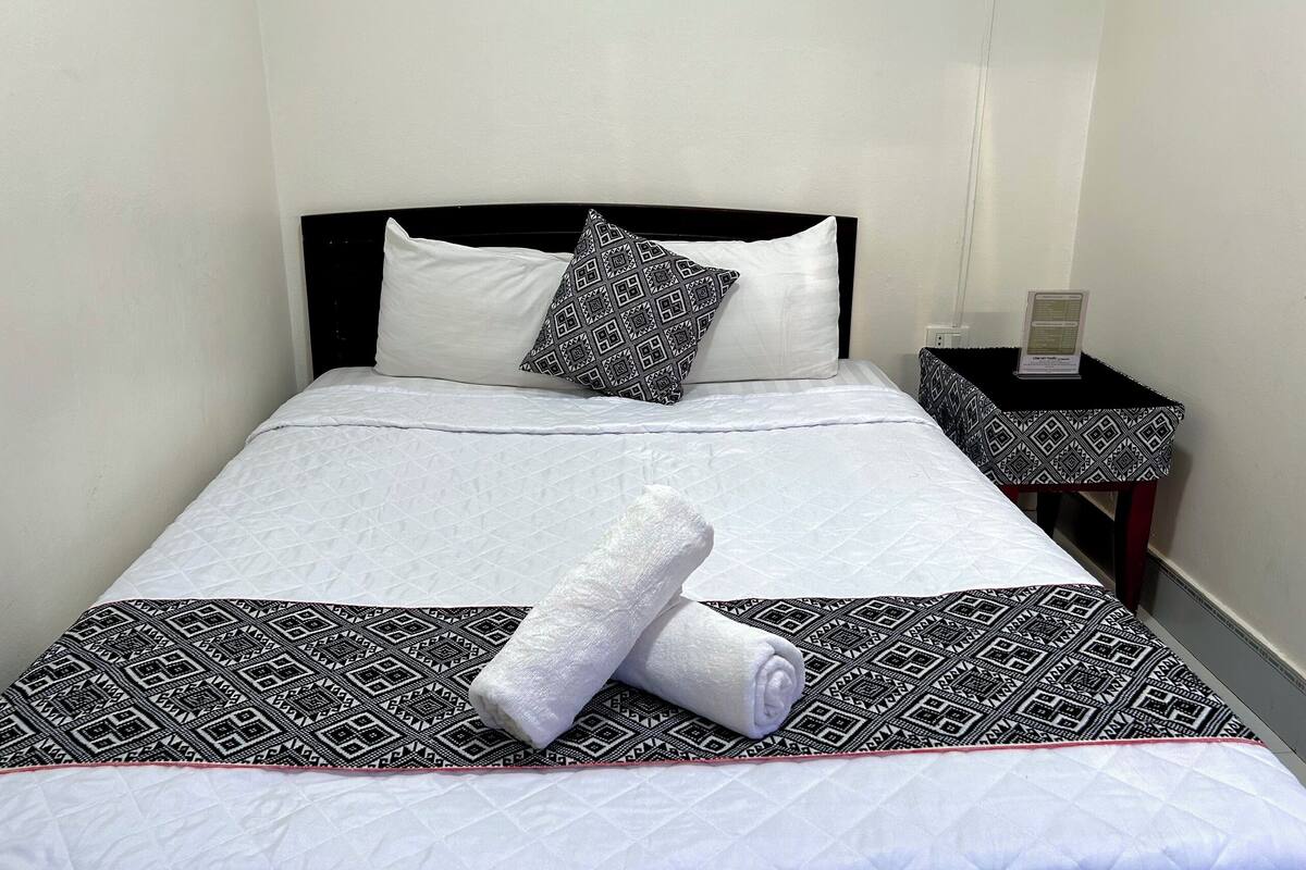 Cama bem arrumada com colcha estampada, um travesseiro e uma toalha enrolada.