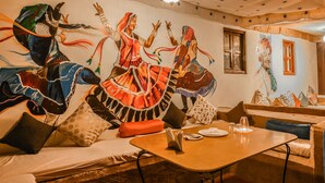 Quarto com um mural de dançarinos, uma mesa de madeira com um cardápio e um sofá com almofadas.