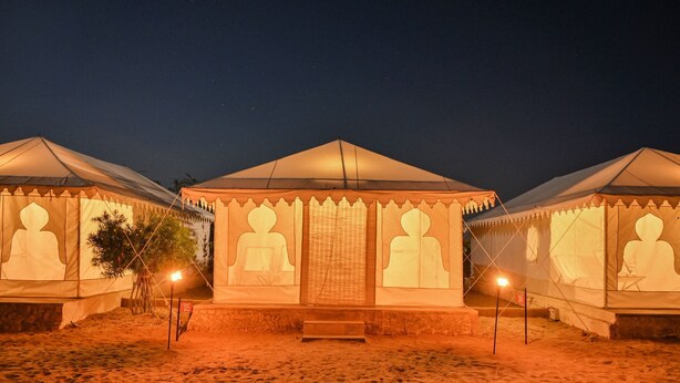 Fileira de tendas com grandes estátuas de Buda nas paredes, em uma área arenosa.