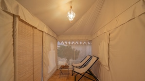 Um quarto com tenda, uma cadeira acolchoada, uma mesa pequena e um candeeiro pendente.