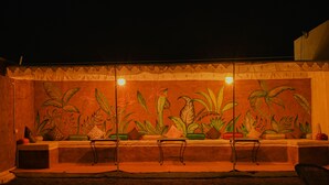 Quarto com um mural de plantas tropicais, uma cama com almofadas e uma pequena mesa.