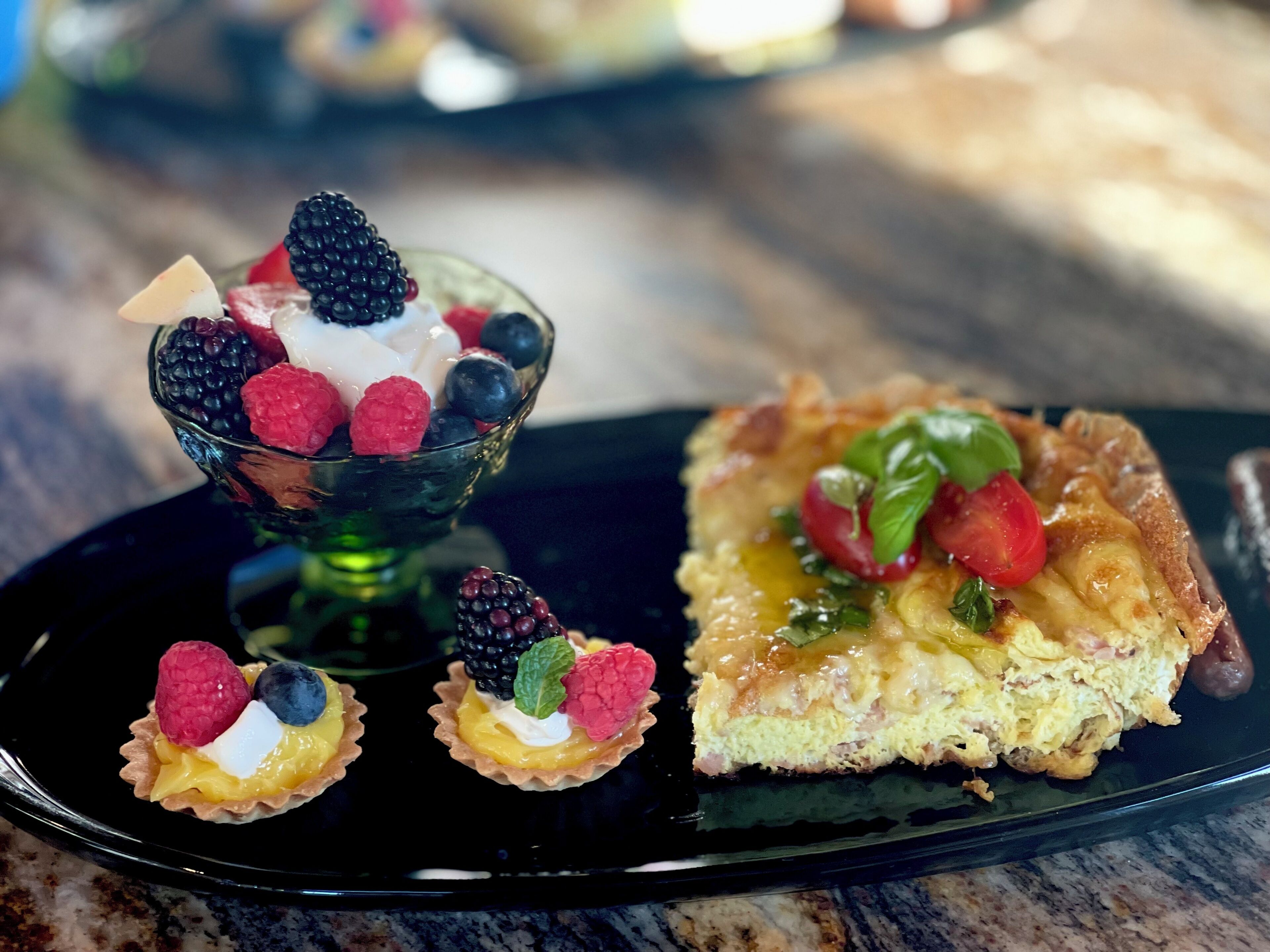 Um prato de sobremesa com uma fatia de quiche e três miniaturas de torta, cada uma coberta com chantilly e frutas vermelhas.
