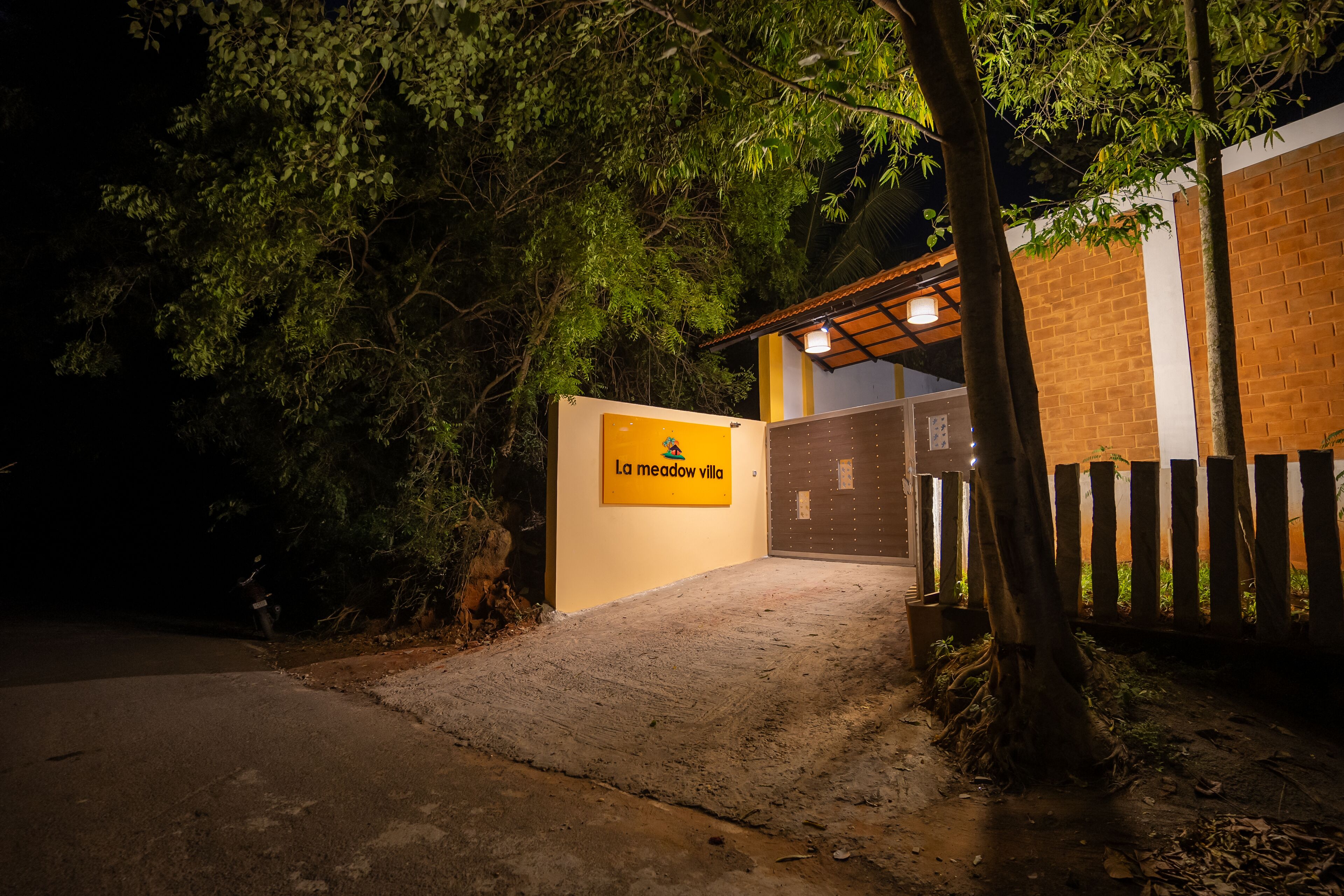 Uma entrada protegida por grades para um terreno chamado "La meadow villa", com um caminho de paralelepípedos que leva a um edifício de tijolos.