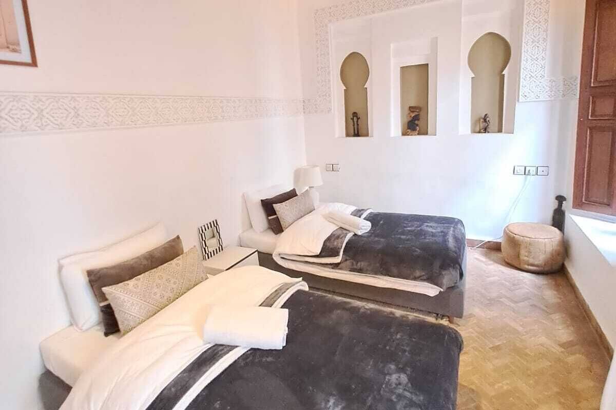 Quarto com duas camas, teto de madeira e parede com três janelas em arco.