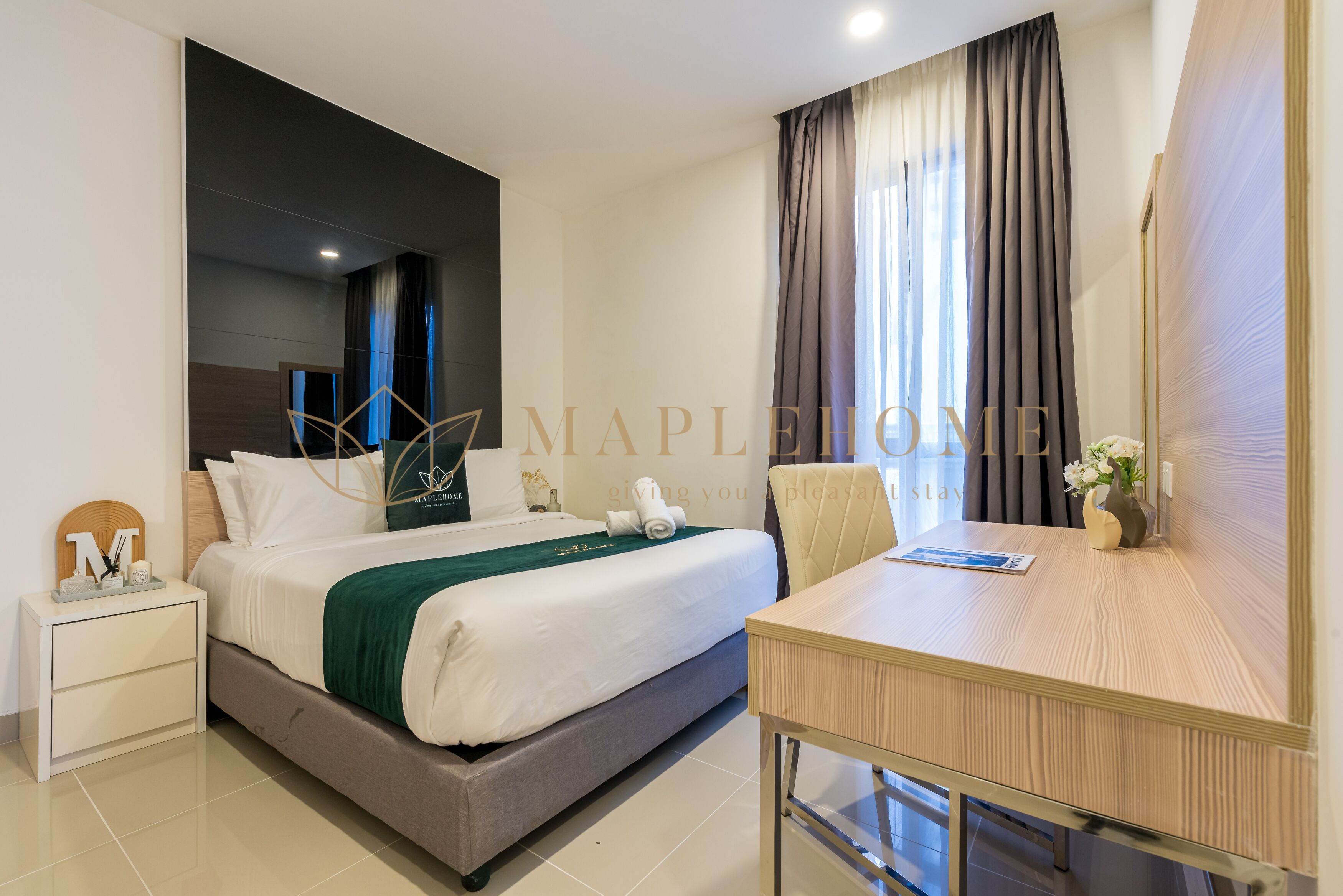 Quarto de hotel moderno com cama bem arrumada, escrivaninha de madeira e uma janela grande com cortinas.
