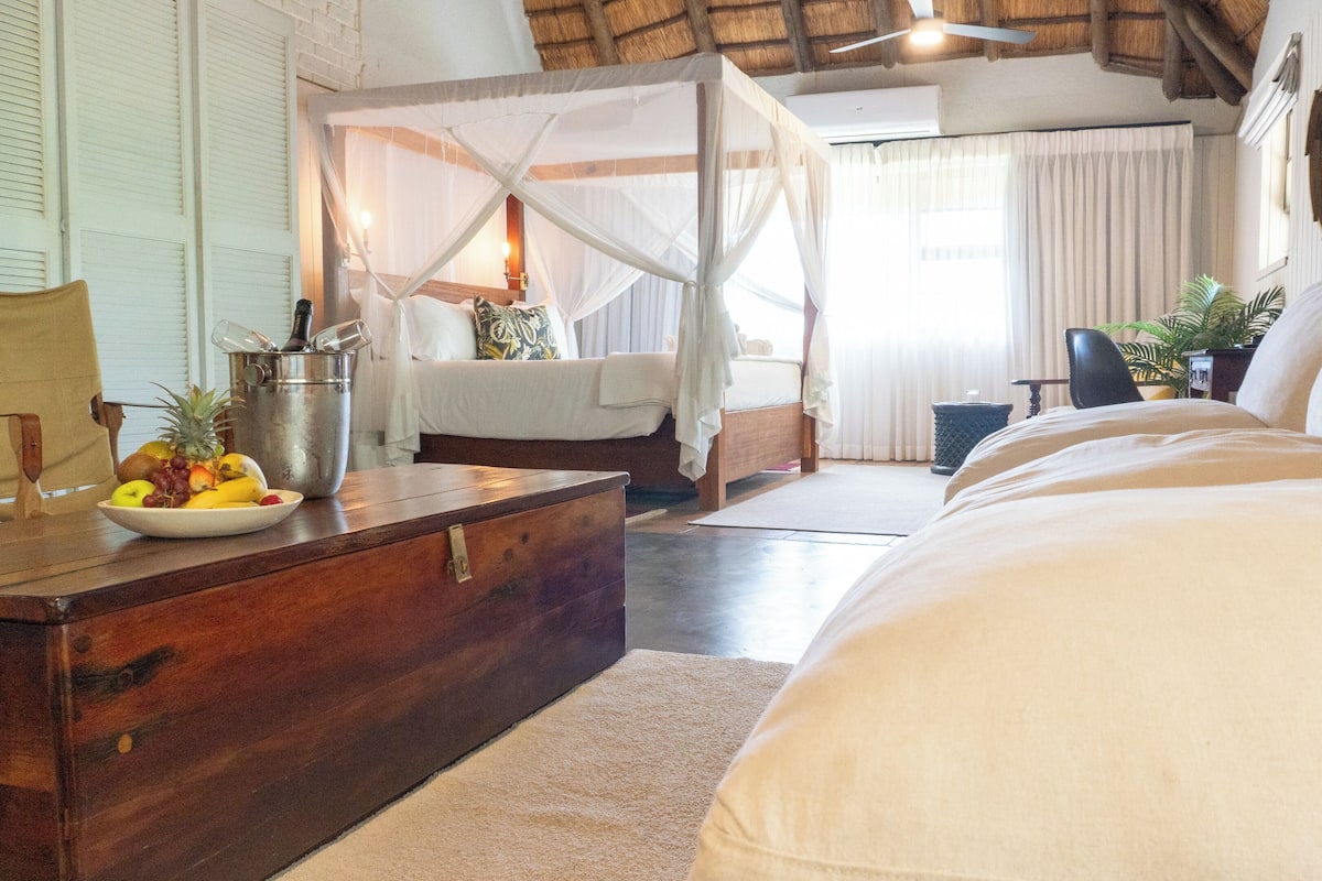 Um quarto com penteadeira de madeira, cama com roupa de cama branca, fruteira e cama com dossel, além de vista para o exterior.