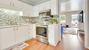 Uma cozinha moderna com armários brancos, forno de aço inoxidável e micro-ondas.
