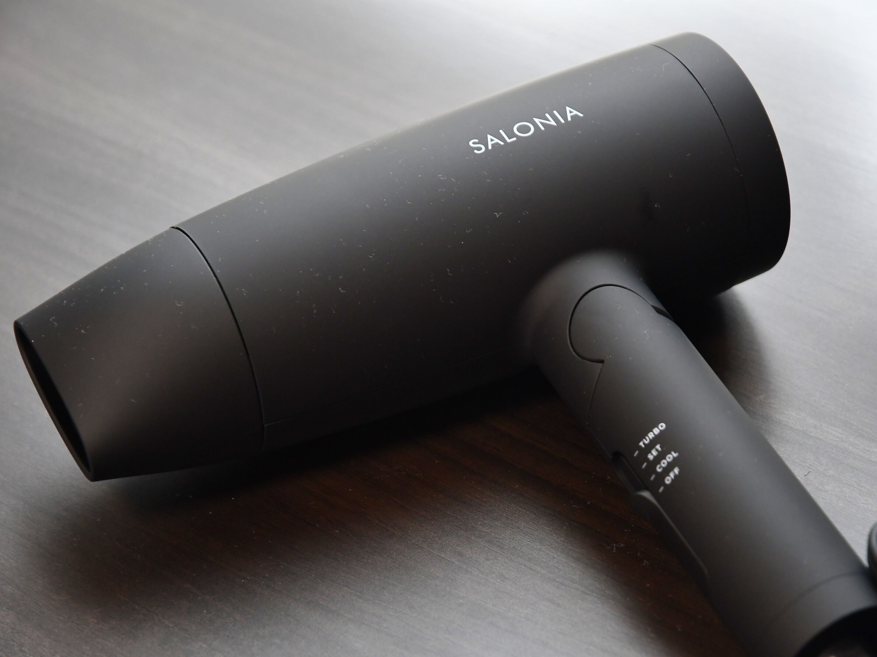 Secador de cabelo preto com a marca 'SALONIA', apoiado em uma superfície de madeira.