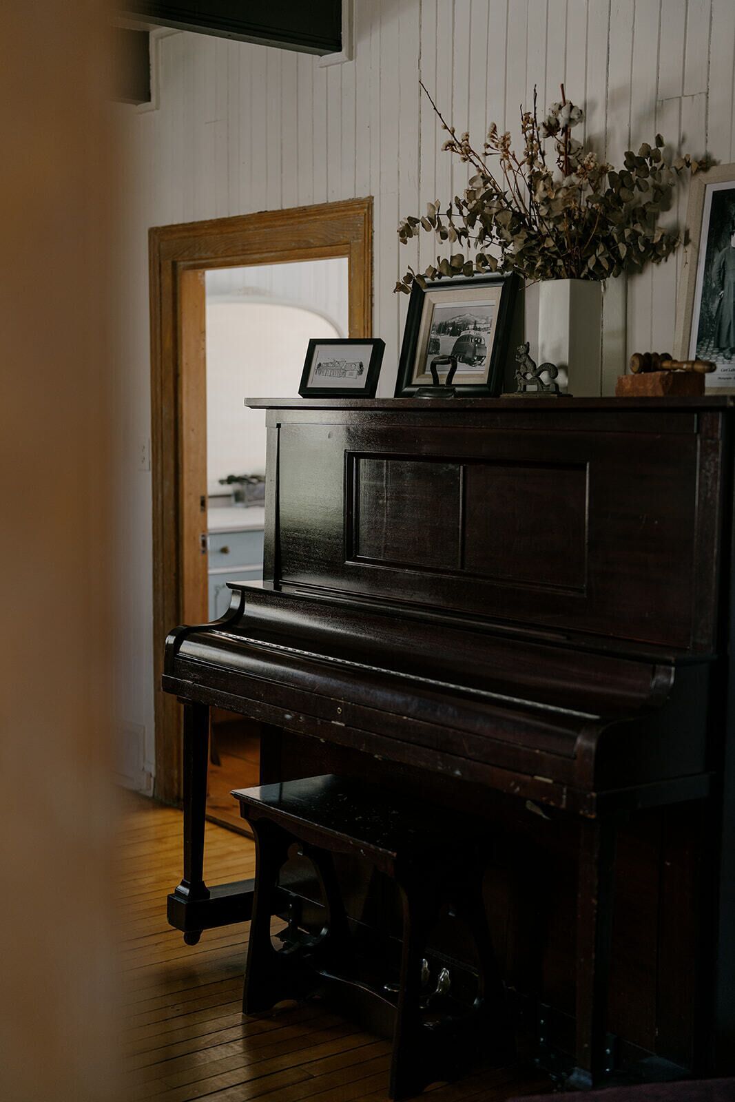 Um piano de madeira em um quarto com paredes de painéis brancos e piso de madeira.