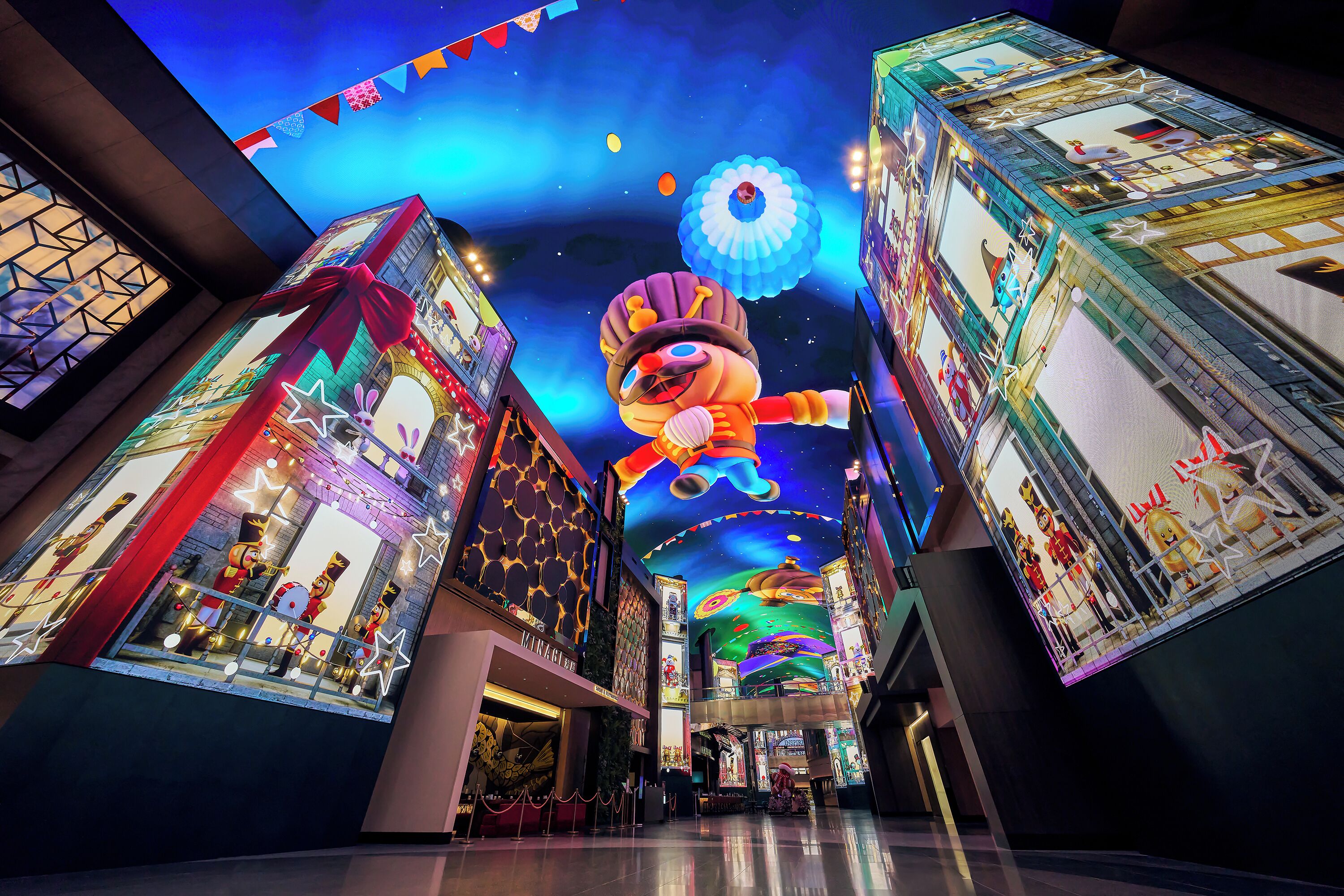 Espaço interno bem iluminado com um grande mural colorido no teto e paredes, retratando diversos personagens e cenas.
