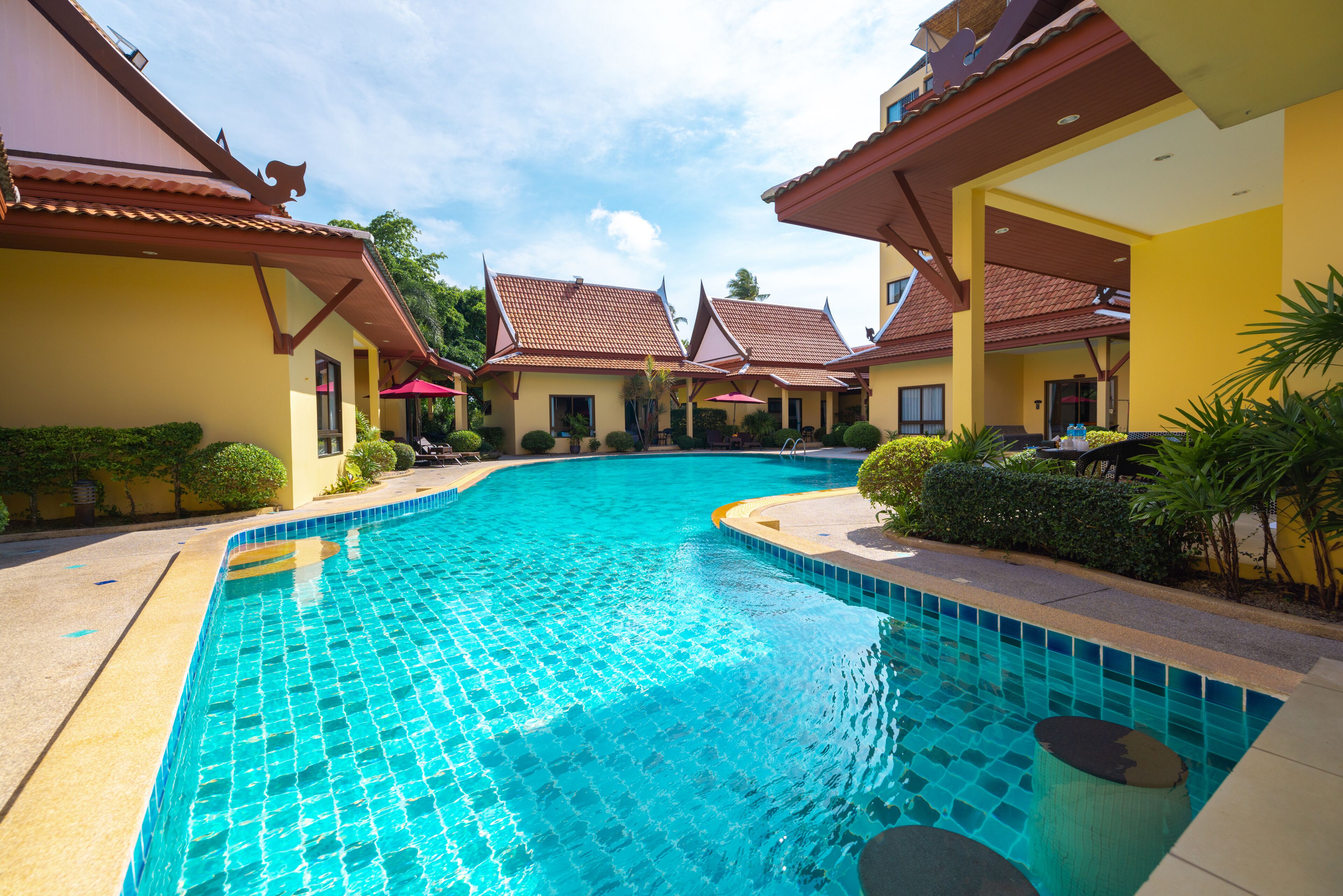 Piscina rodeada por edifícios amarelos com telhados vermelhos, alguns com guarda-sóis.