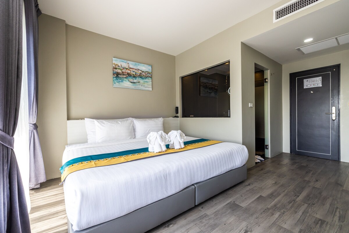 Quarto de hotel com cama, um quadro, uma porta e uma janela com cortinas.