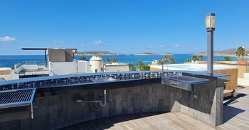 Cozinha externa com vista para o mar, piscina e montanha ao fundo.