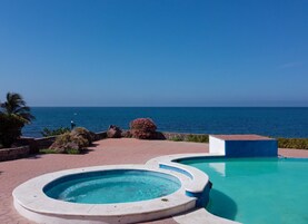 Uma piscina com design curvo, ladeada por um caminho de pedra e vista para o oceano.