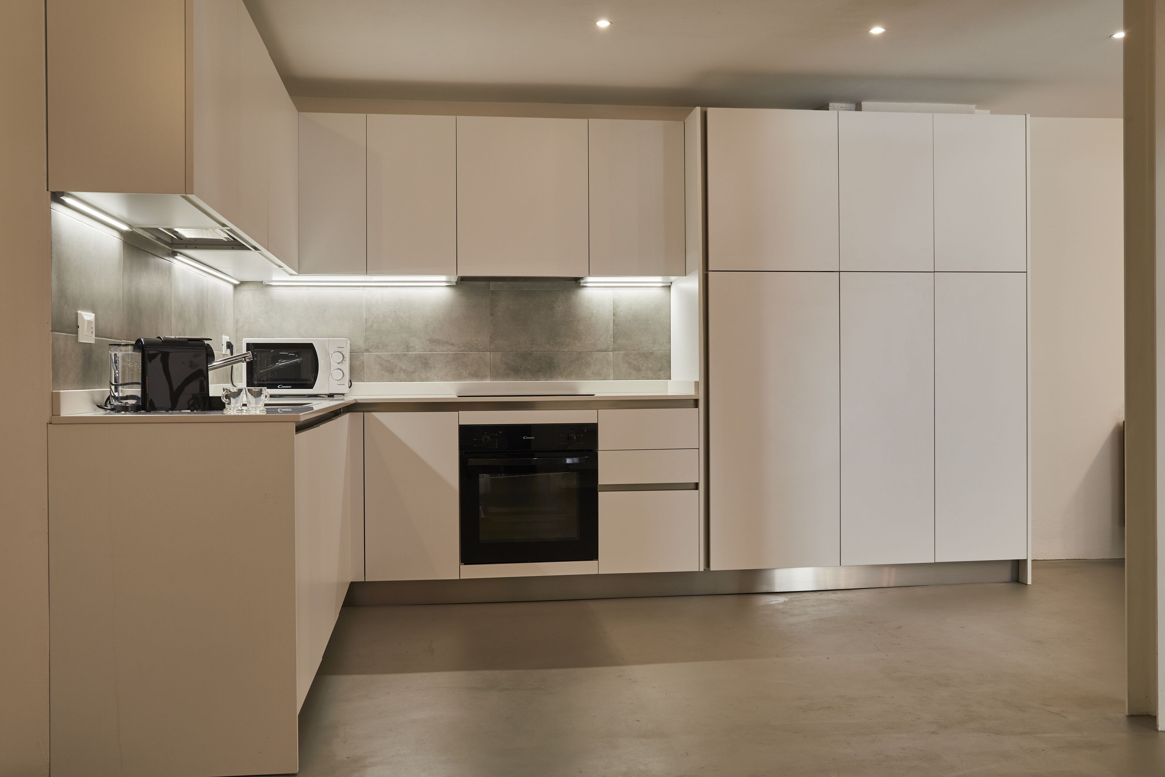 Uma cozinha moderna com armários brancos, forno embutido e micro-ondas.